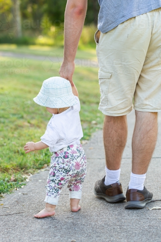 Image of Barefoot baby walking down path holding dad's hand - Austockphoto
