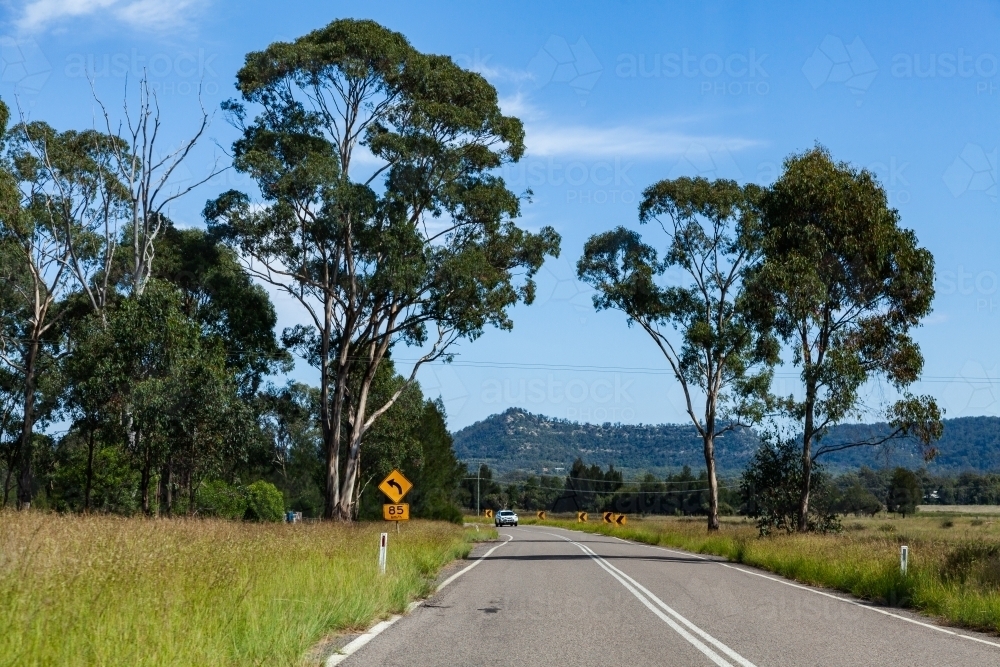 Image of Bend in road ahead slow down sign beside highway - Austockphoto