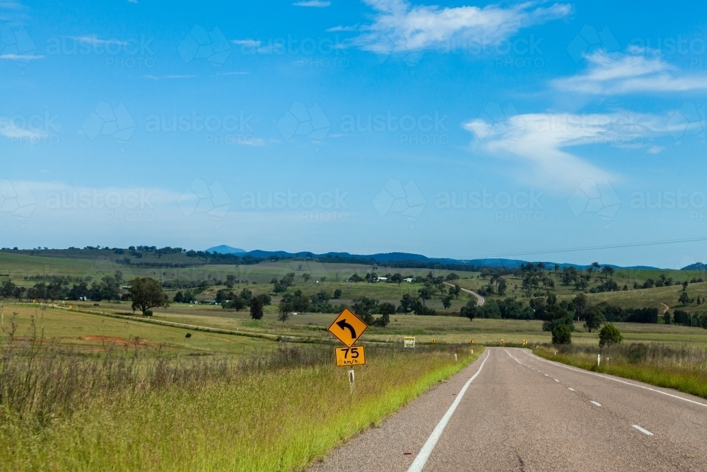 Image of Bend in road ahead slow down sign beside highway - Austockphoto
