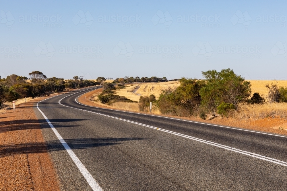 Image of Bitumen road through dry landscape with blue sky - Austockphoto