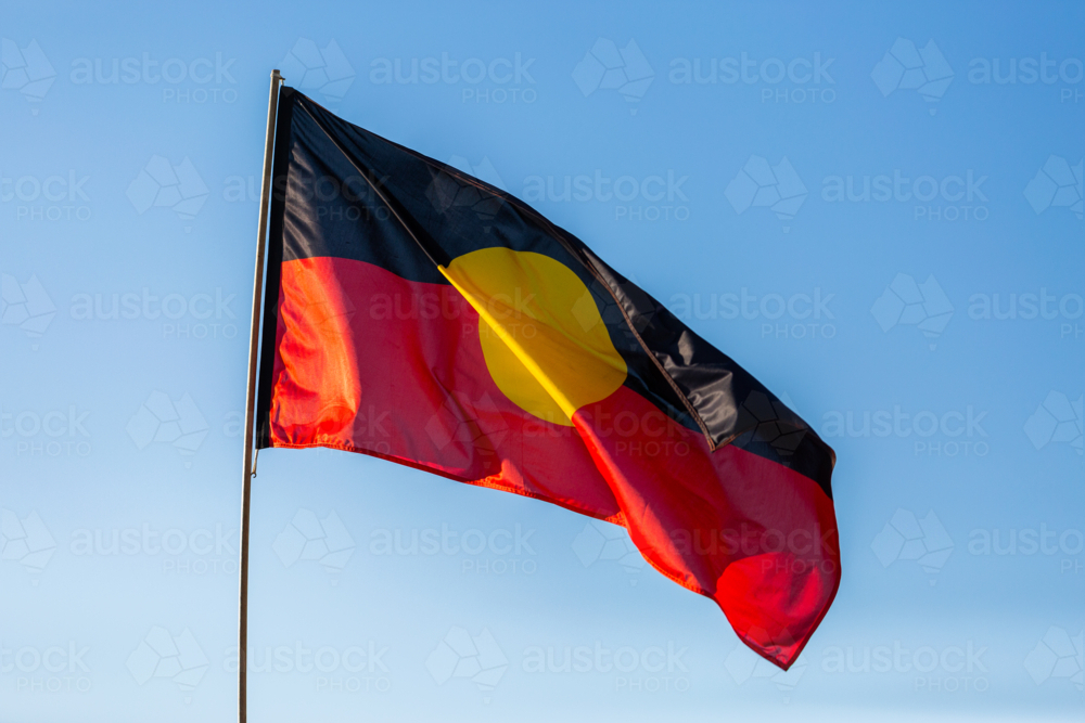 Image of Black yellow and red Aboriginal flag flying in blue sky - Austockphoto