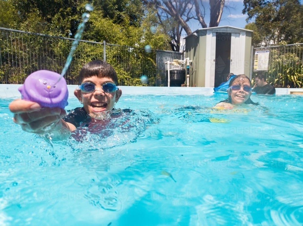 Image of Boy and girl in backyard pool having water fight - Austockphoto
