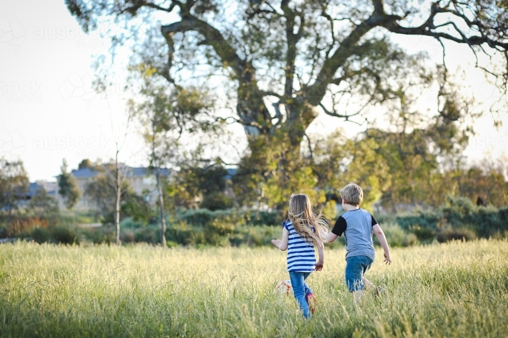 Image of Boy and girl running through long grass playing soccer at the ...