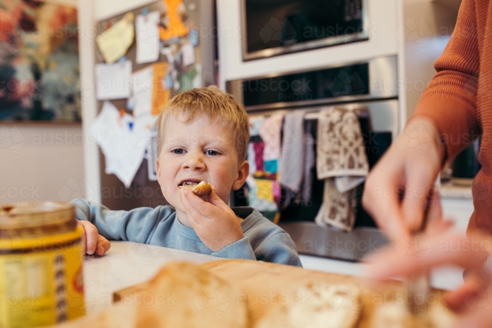 Image of Boy eating bread while parent slices loaf - Austockphoto