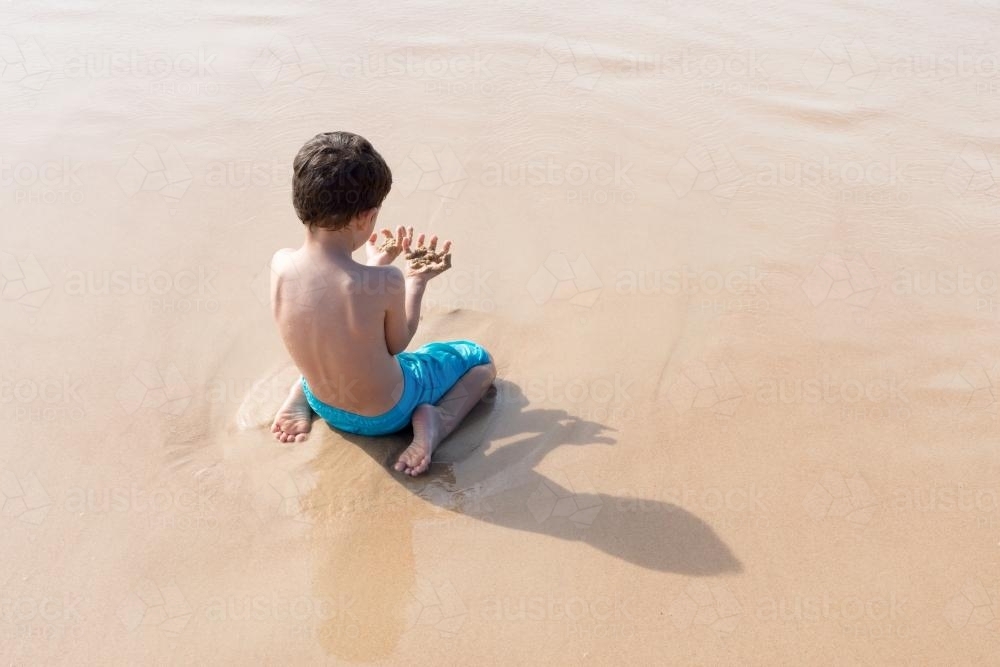 Image of Boy kneeling on sand by the seashore - Austockphoto