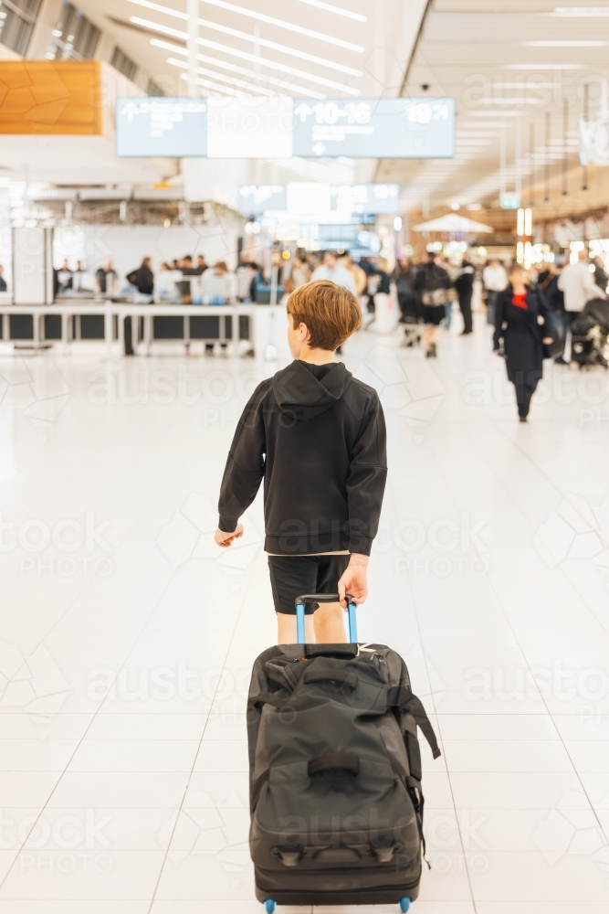 Image of Boy pulling rolling suitcase through airport terminal ...