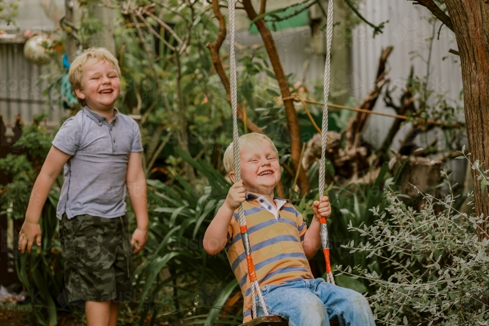 Image of Boy pushing little brother on swing - Austockphoto