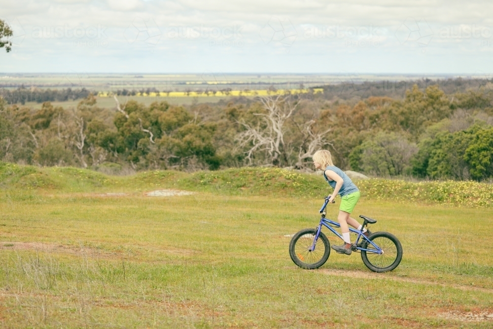 Image of Boy riding bike in on hill with farmland in distance ...