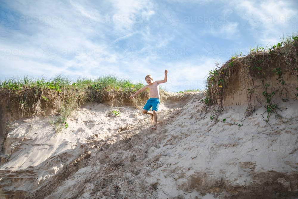 Image of Boy running down sand dunes at the beach - Austockphoto
