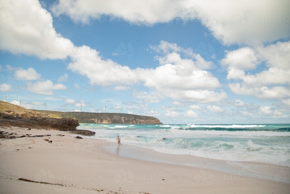 Image of Boy running from waves on the beach with wind turbines on ...