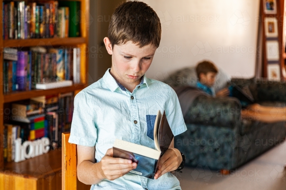 Image of Boy sitting on kitchen stool reading a book - Austockphoto