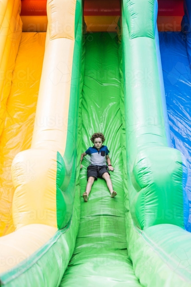 Image of Boy sliding down blow up slide at local show - Austockphoto