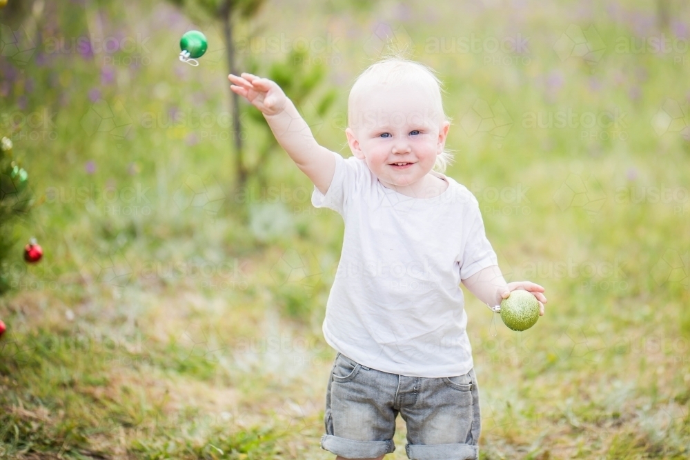 Image of Boy smiling throwing Christmas bauble outdoors - Austockphoto