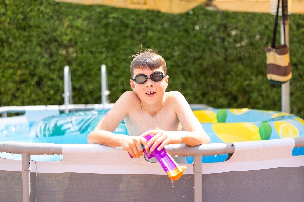 Image of Boy swimming in backyard pool with water pistol on summer day ...