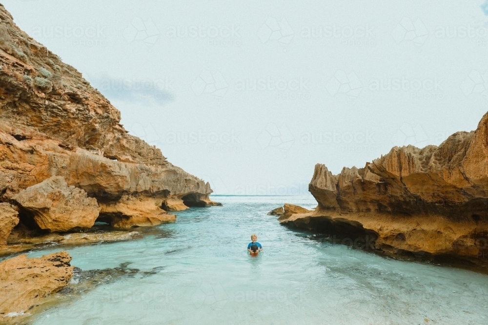 Image of Boy swimming in beach cove between large sandstone rock cliffs ...