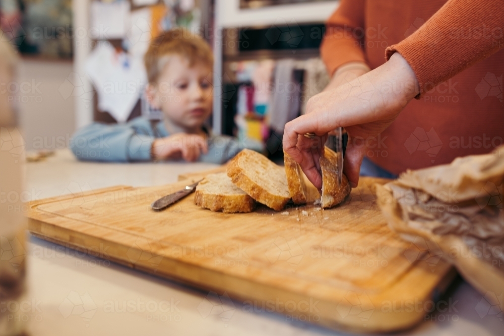 Image of Boy waiting at kitchen bench while parent slices bread ...