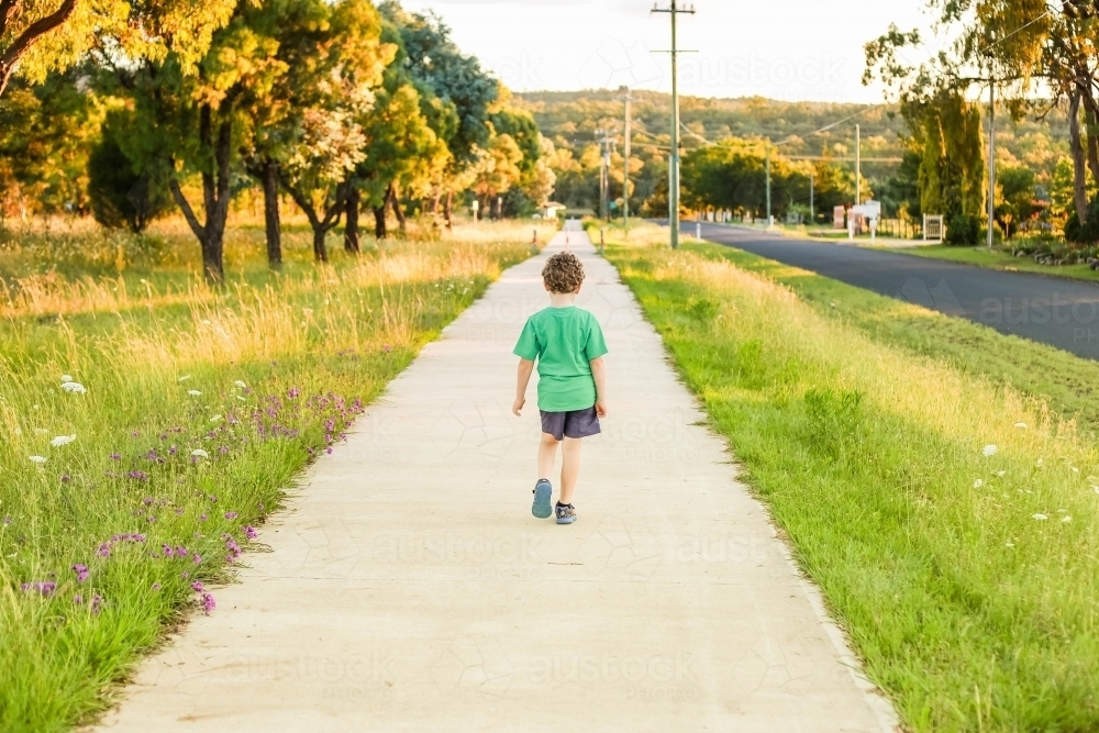Image of Boy walking down concrete path with green grass and trees ...