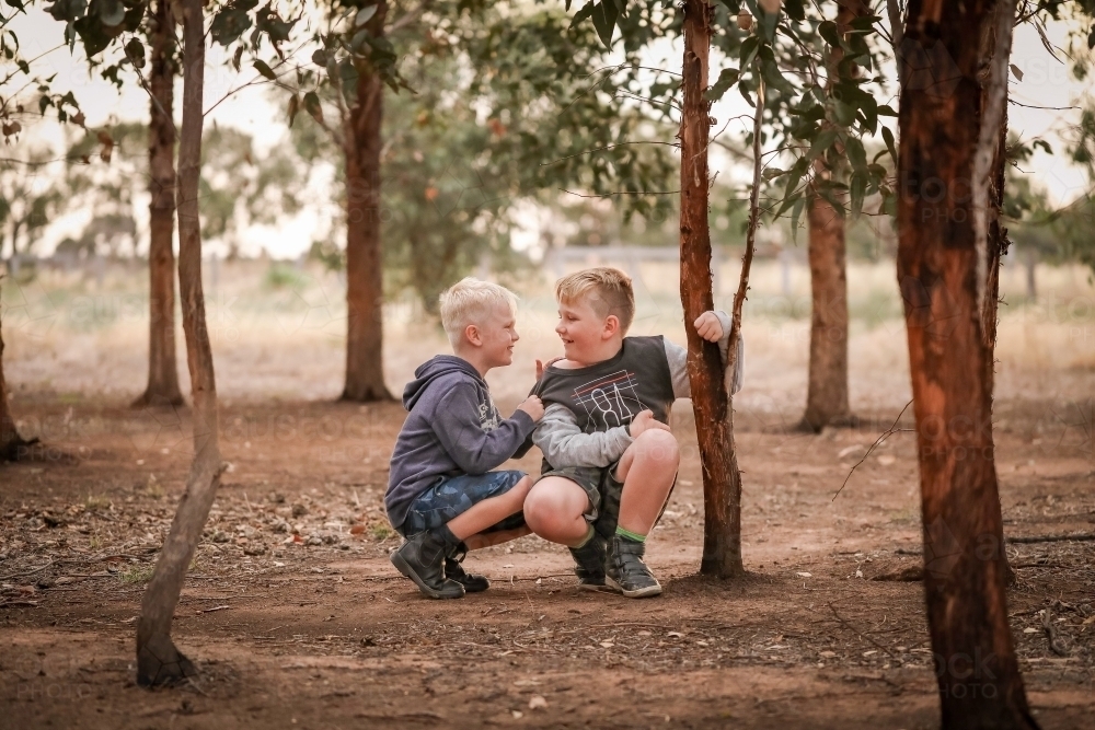 Image of Boys squatting down among trees smiling at each other ...