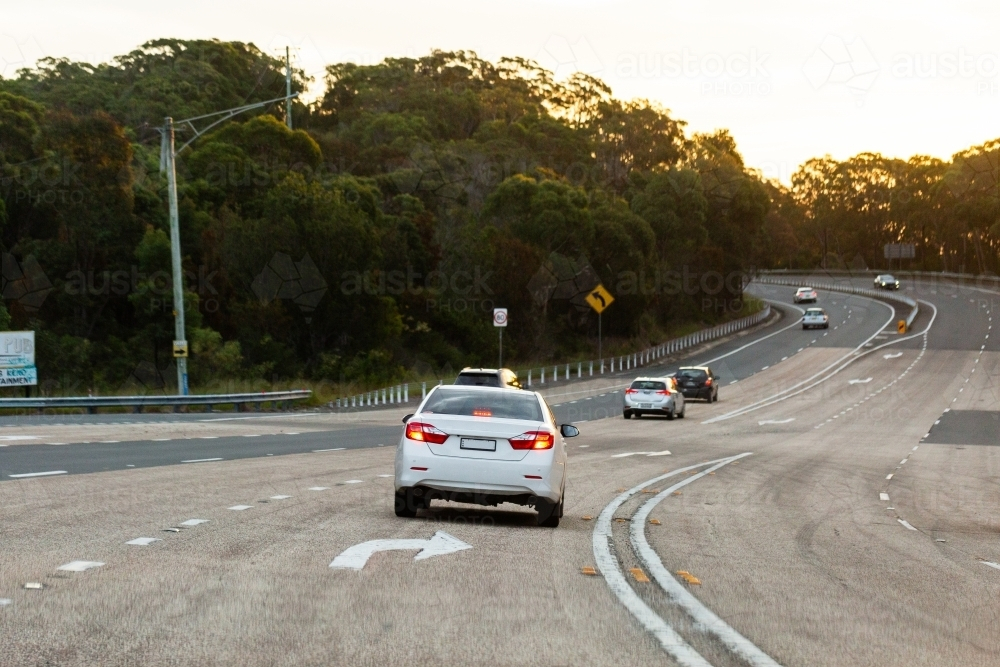 Image of can in turning lane of wide road between suburbs in evening ...