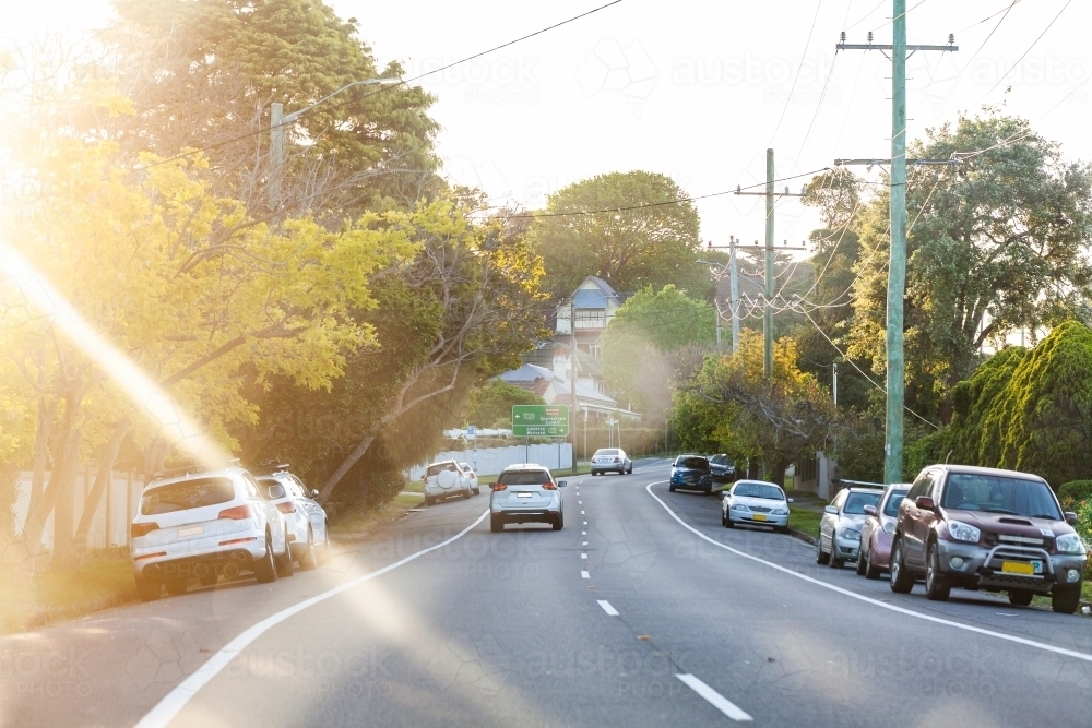 Image of Car driving down road with parked cars beside in afternoon ...
