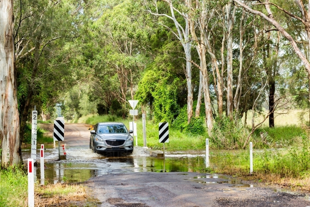 Image of Car driving over level crossing causeway covered in floodwater ...