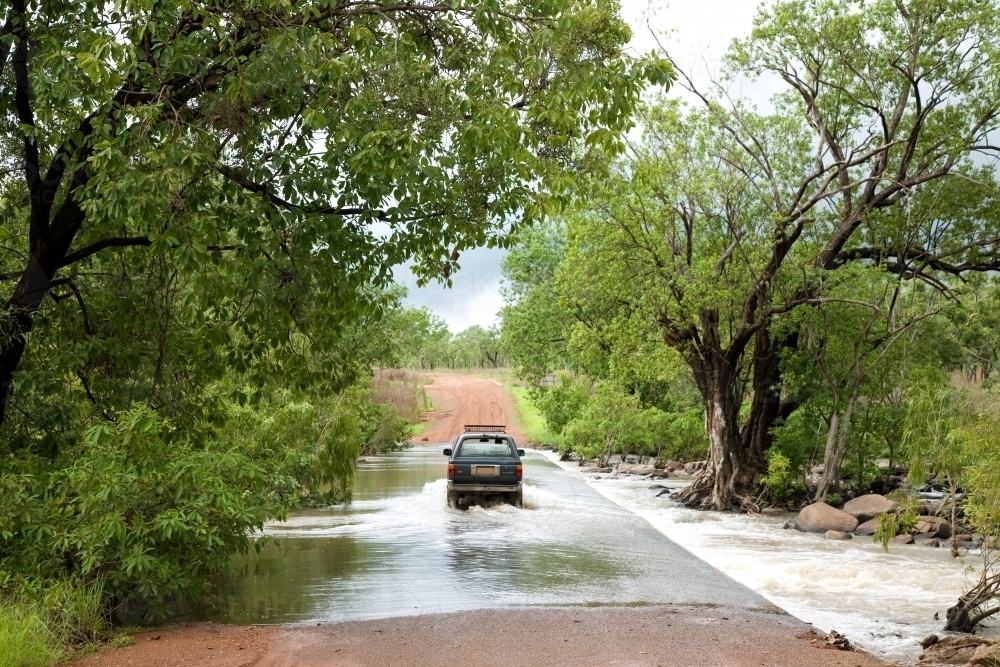 Image of Car driving through flooding on dirt road surrounded by green ...