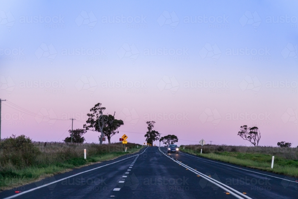 Image of car with headlights driving on country road at dusk - Austockphoto
