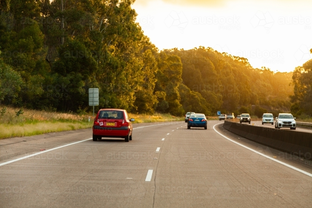 Image of Cars driving down highway road at sunset - Austockphoto