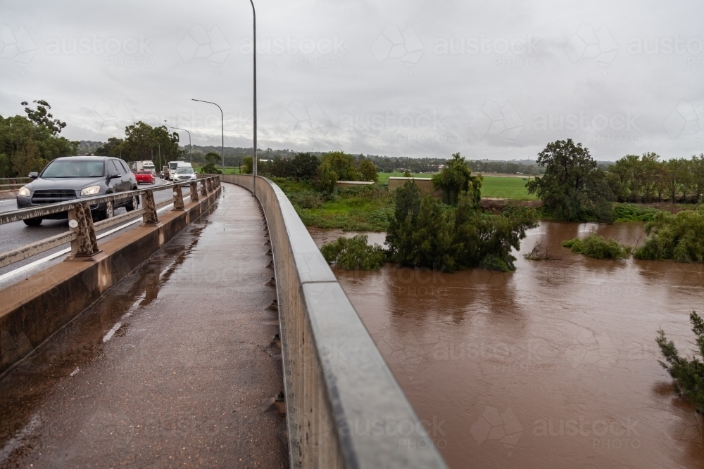Image of Cars driving over bridge in wet weather with flooding river ...