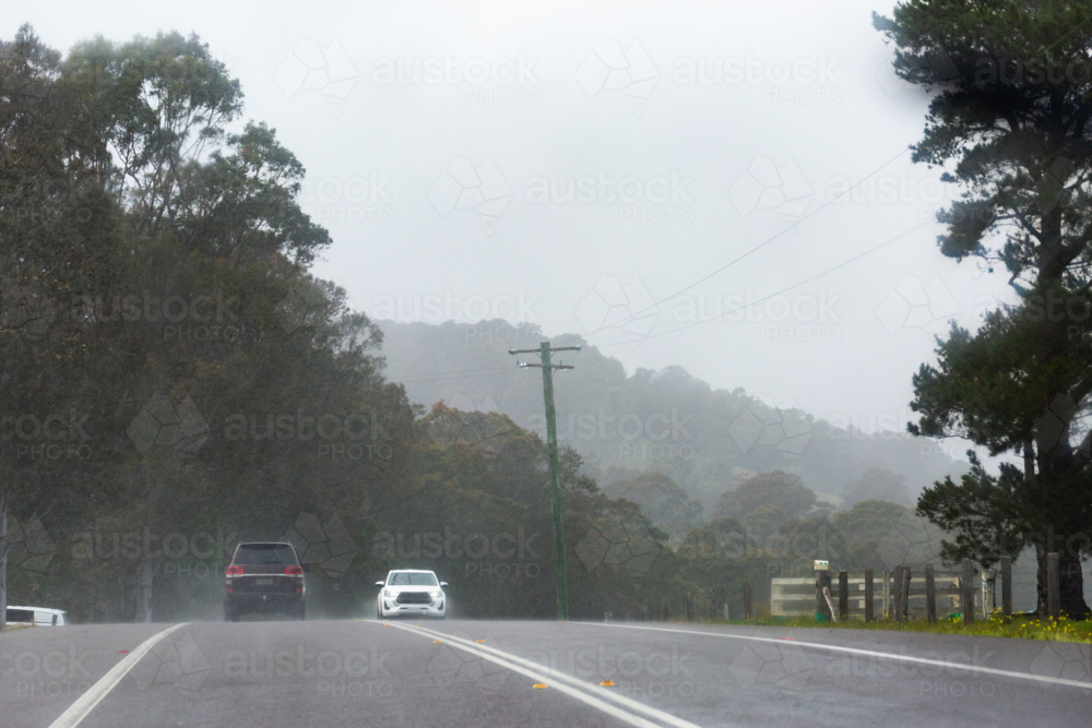Image of Cars passing on rural road in heavy rain - Austockphoto