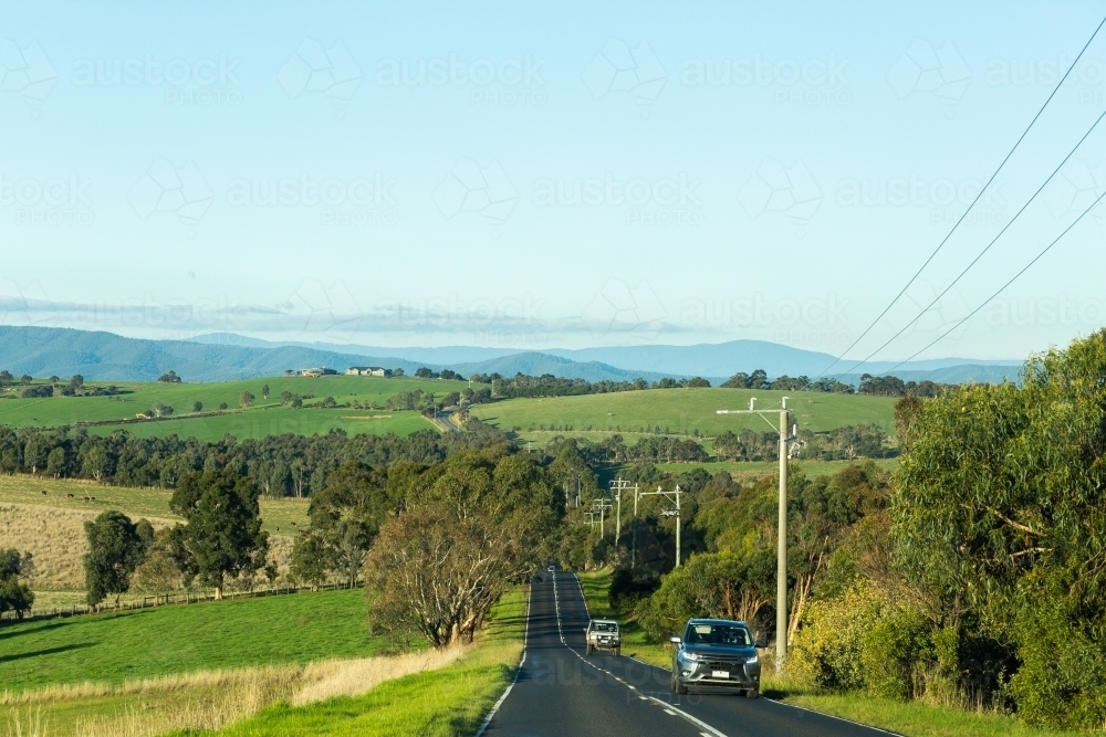 Image of Cars traveling down road in green countryside - Austockphoto