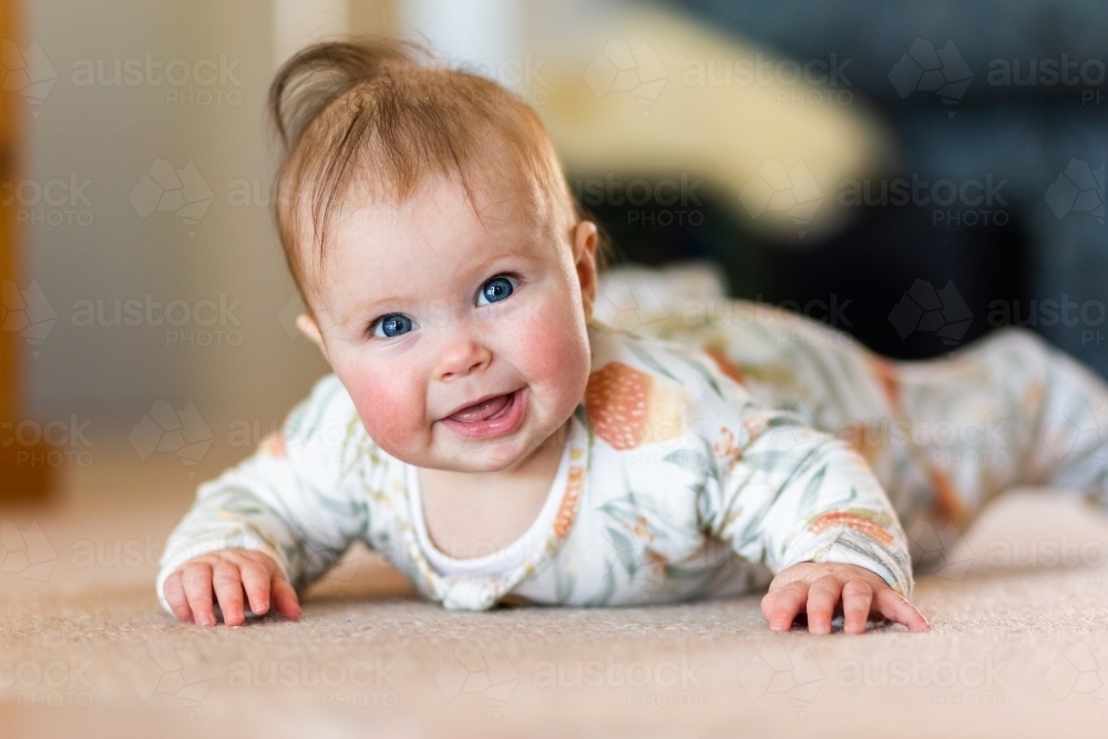 Image of cheeky baby doing tummy time on loungeroom floor - Austockphoto