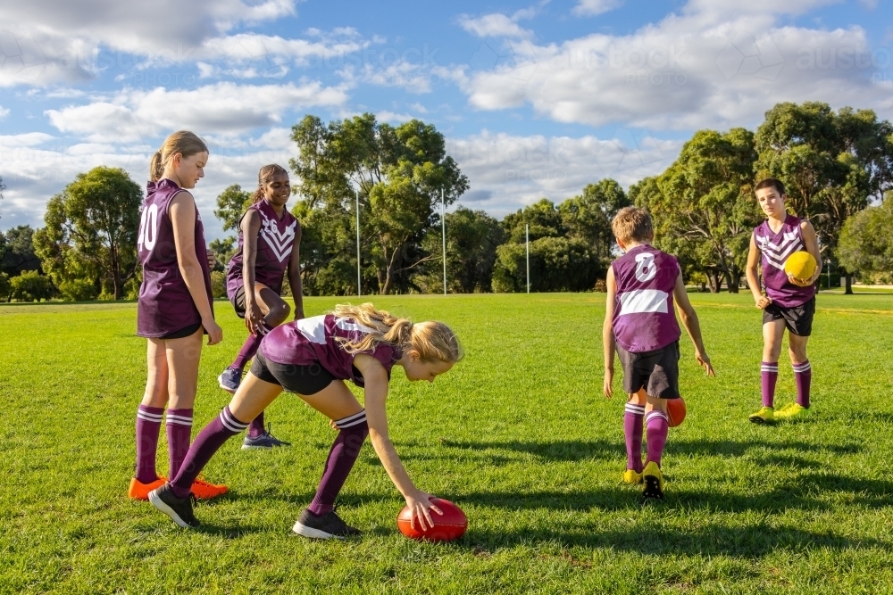 Image of child bending to pick up afl football with teammates at ...