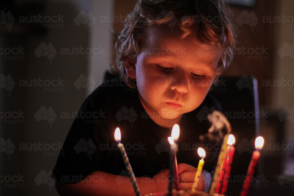 Image of Child blowing out birthday cake candles in dark room ...
