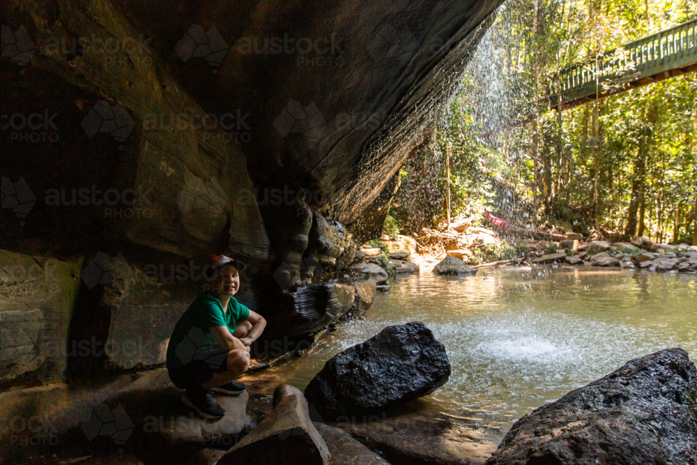 Image of Child crouched in a cave behind a waterfall - Austockphoto