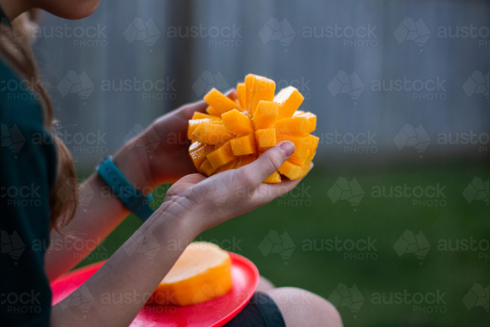 Image of child eating a cheek of fresh sliced mango - Austockphoto