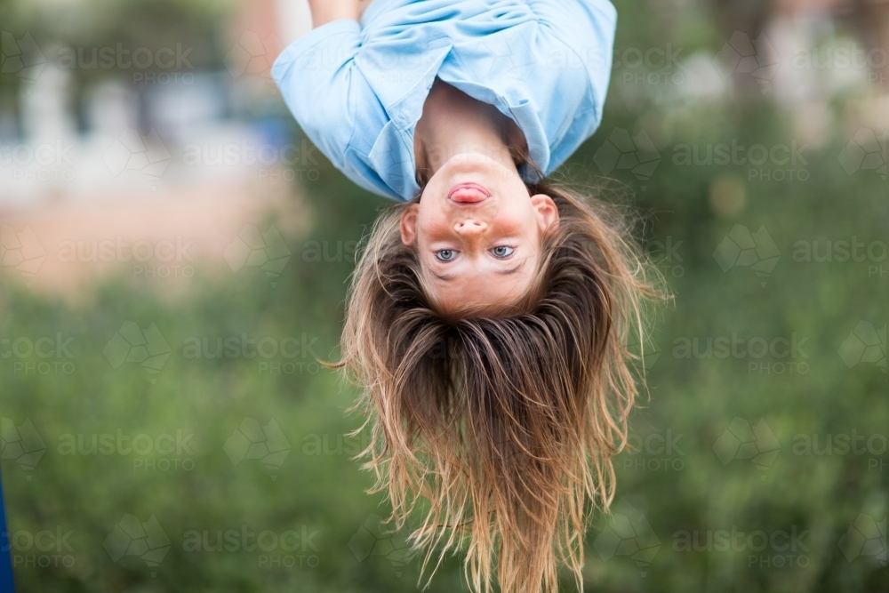 Image of Child hanging upside downing poking tongue - Austockphoto