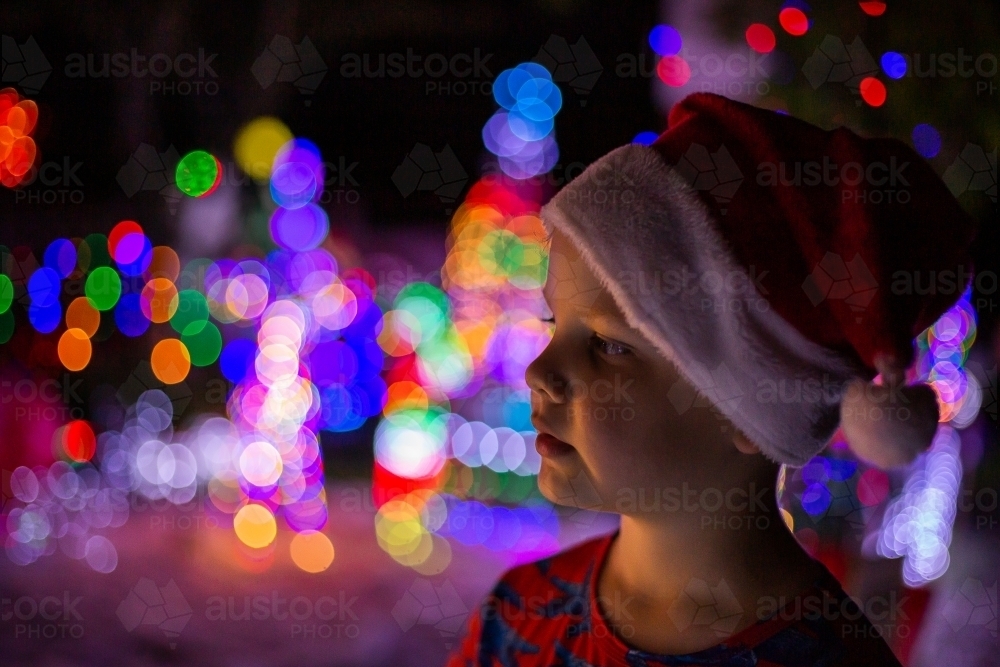 Image of child in a santa hat looking at colourful christmas lights ...