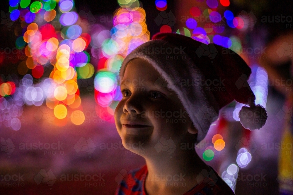 Image of child wearing santa hat looking at Christmas lights - Austockphoto