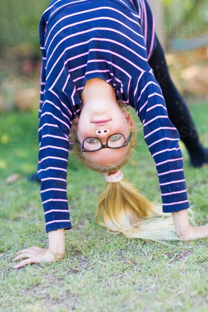 Image of Child with blonde hair in ponytail doing a bend back on grass ...