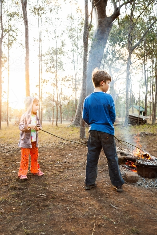 Image of Children poking sticks into campfire at campsite - Austockphoto