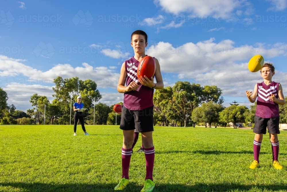 Image of children with afl footballs and their coach on the background ...