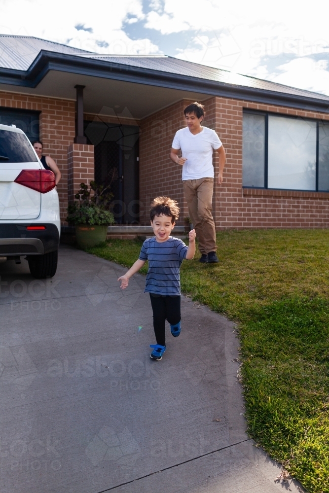 Image of Chinese Australian dad running after boy playing in front yard ...