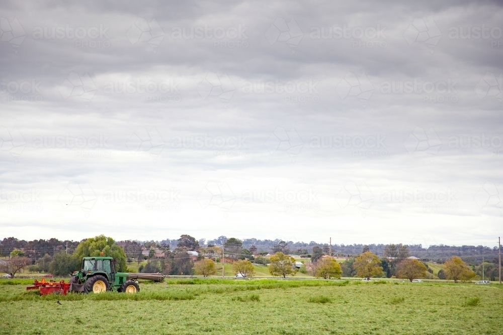 Image of Green tractor pulling red slasher in lucerne paddock ...