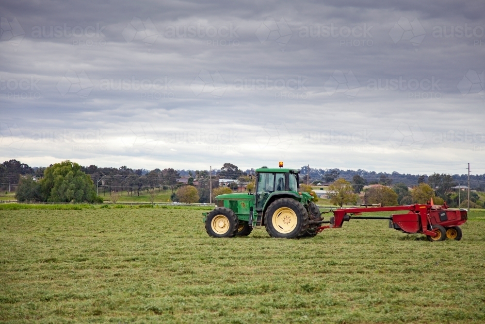 Image of Green tractor pulling red slasher in lucerne paddock ...