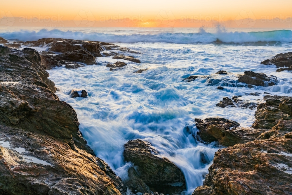 Image of Close up of a waves splashing into a rockpool with a sunrise ...