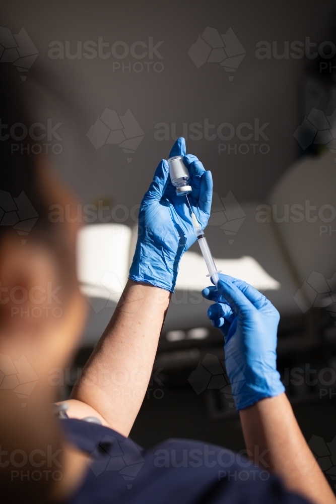 Image of Close up shot of a syringe being inserted to a medicine glass vial by a healthcare ...
