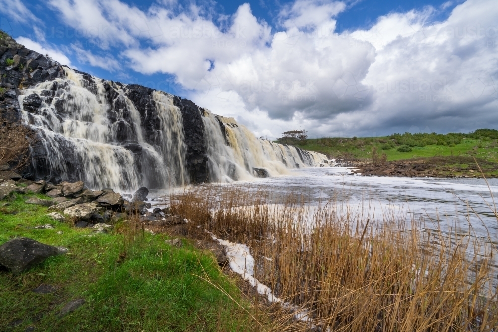 Image of Close up view of a wide waterfall tumbling into a river lined ...