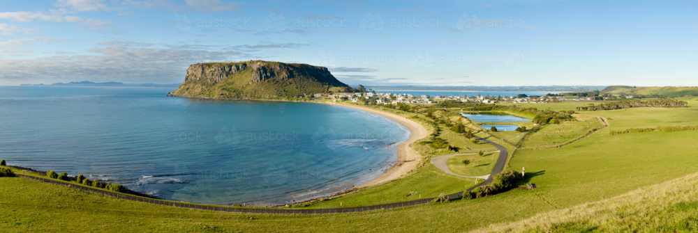 Image of Coastal cliff rising above a calm curving bay and green ...