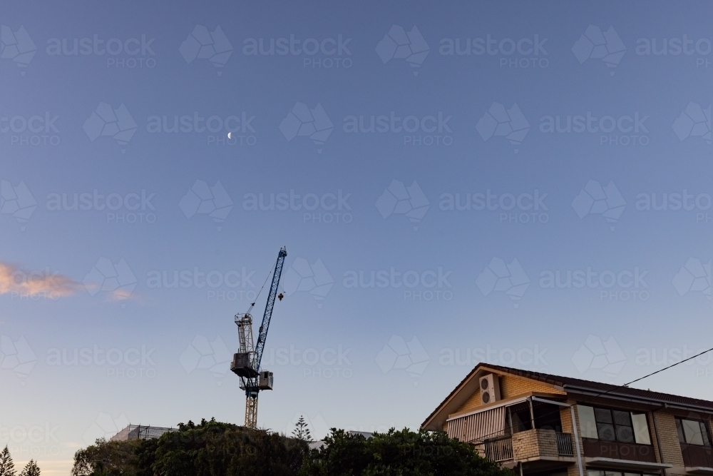 Image of Construction crane rising above buildings in twilight sky ...